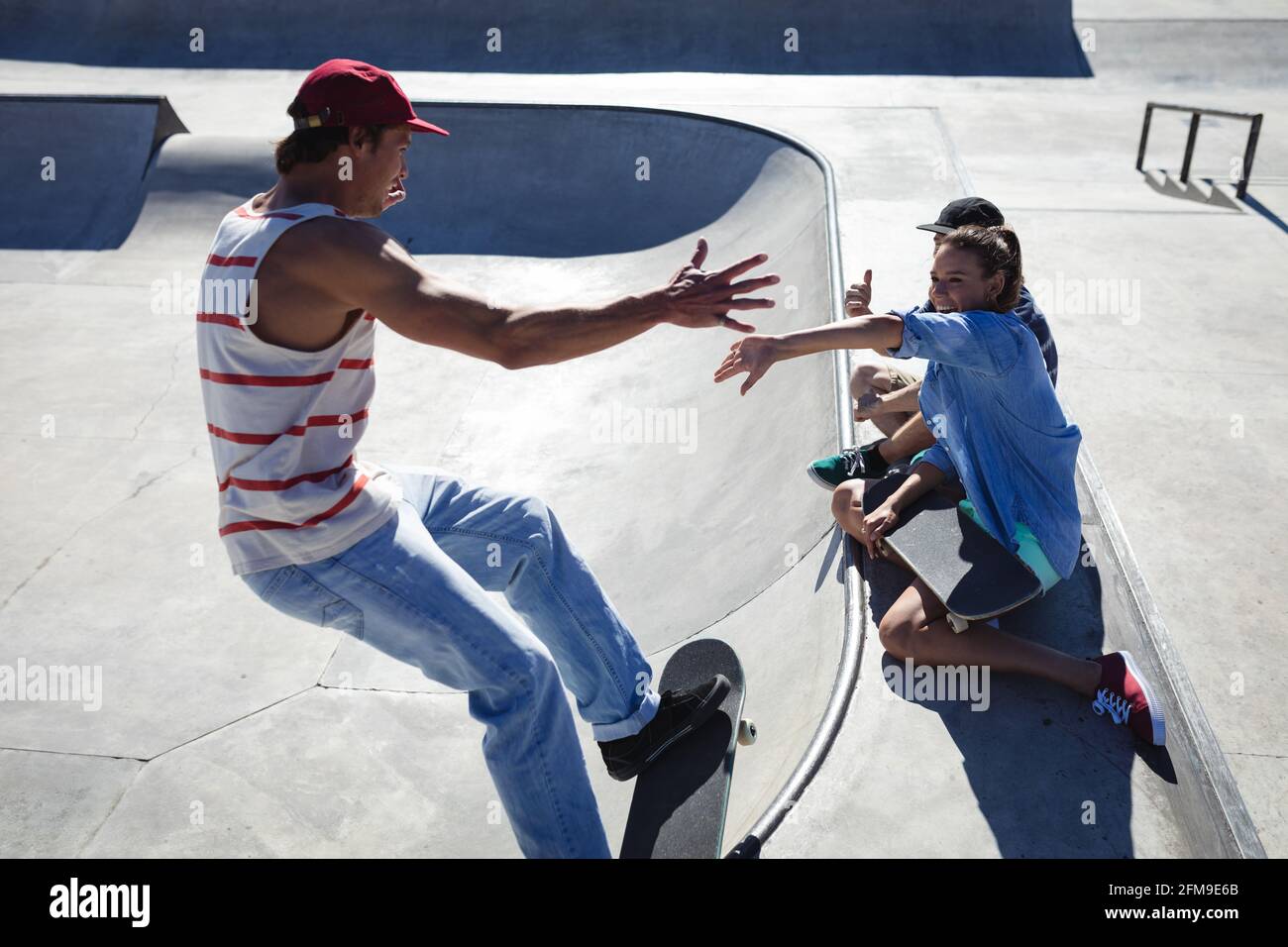 Three happy caucasian female and male friends skateboarding in the sun ...