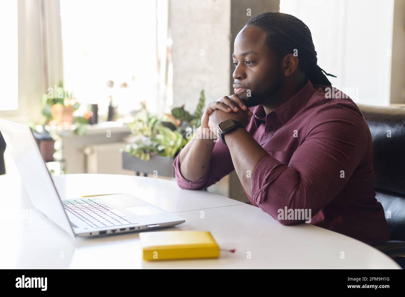 Focused and concerned black man in smart casual shirt looks at laptop ...