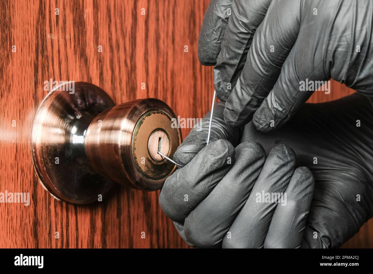 Thief in black gloves opens a wooden door with a simple lock using an ...