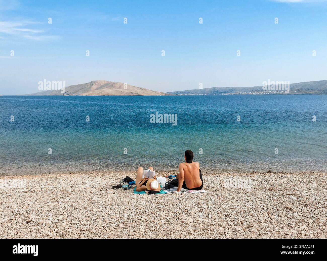 Rear view of young couple sitting on beach with amazing view of sea and ...
