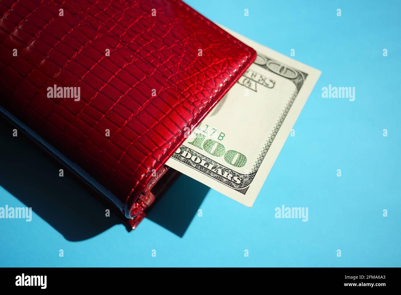 Hundred dollar bill sticking out of a red purse on a bright blue table ...