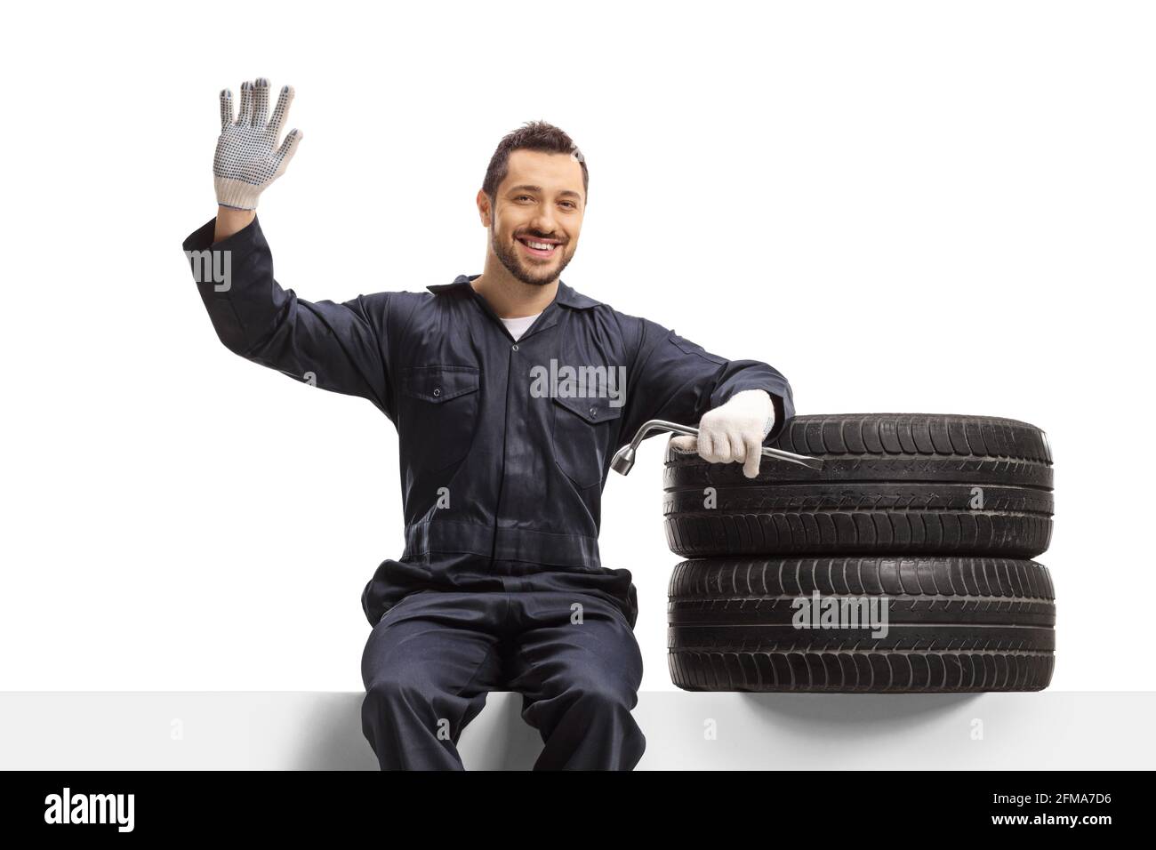 Auto mechanic sitting on a panel with a pile of tires and a wrench and ...