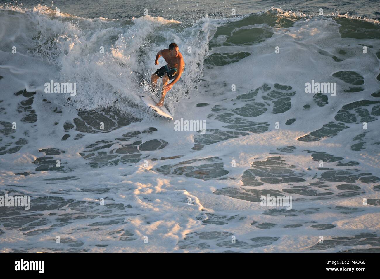 Sunset landscape with a male surfer riding a wave on the coast of ...
