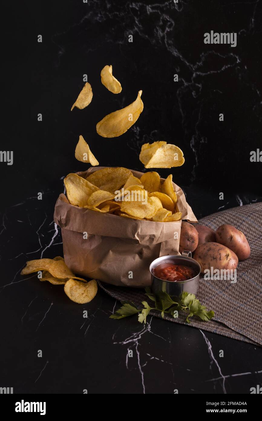 Crispy nachos flying in the air with a sauce and potatoes on a black ...