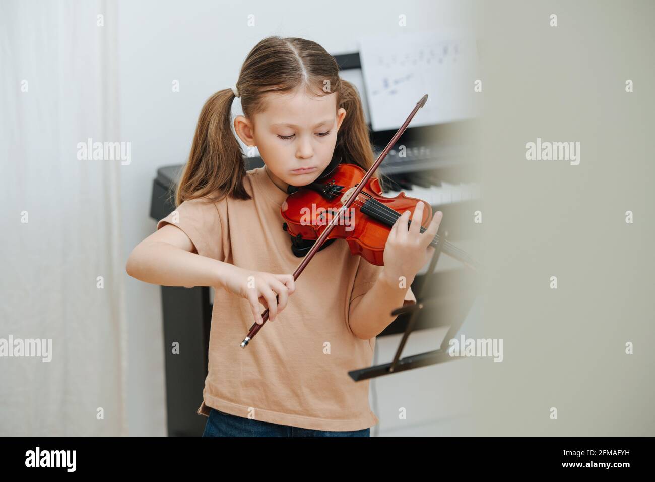 Hard-working little girl with two pony tails learning to play violin ...