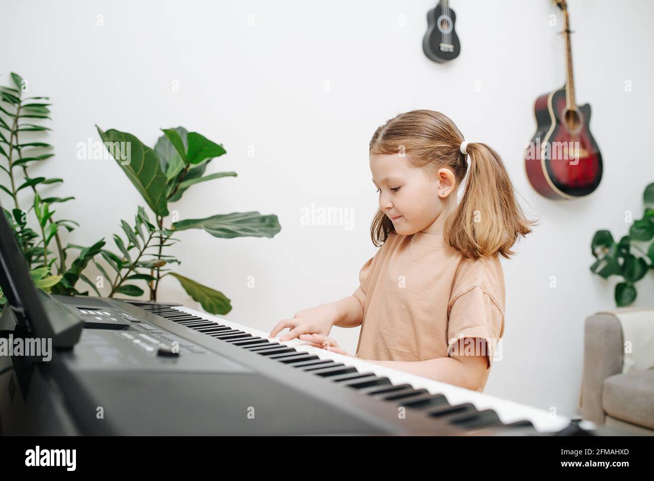 Adorable little girl enjoys playing electric piano at home. Side view ...