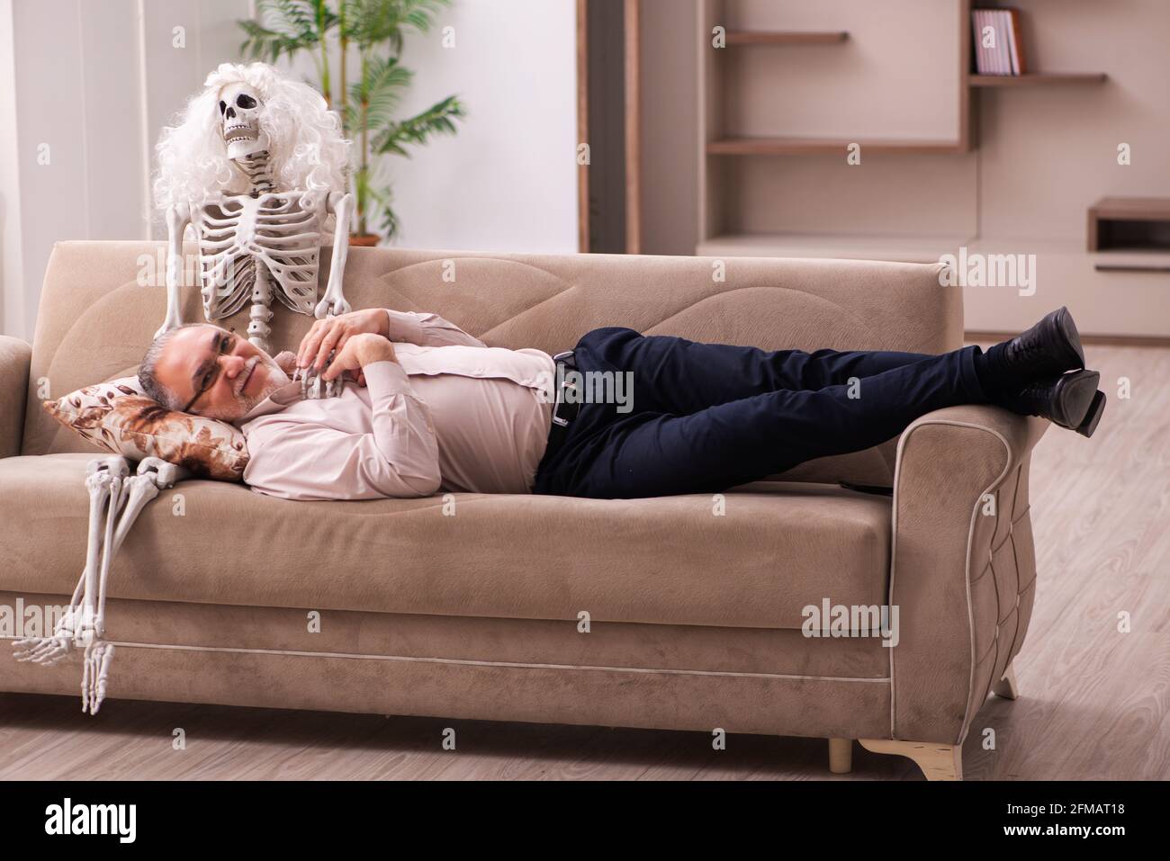 Old man sitting on the sofa with the female skeleton in undying love ...
