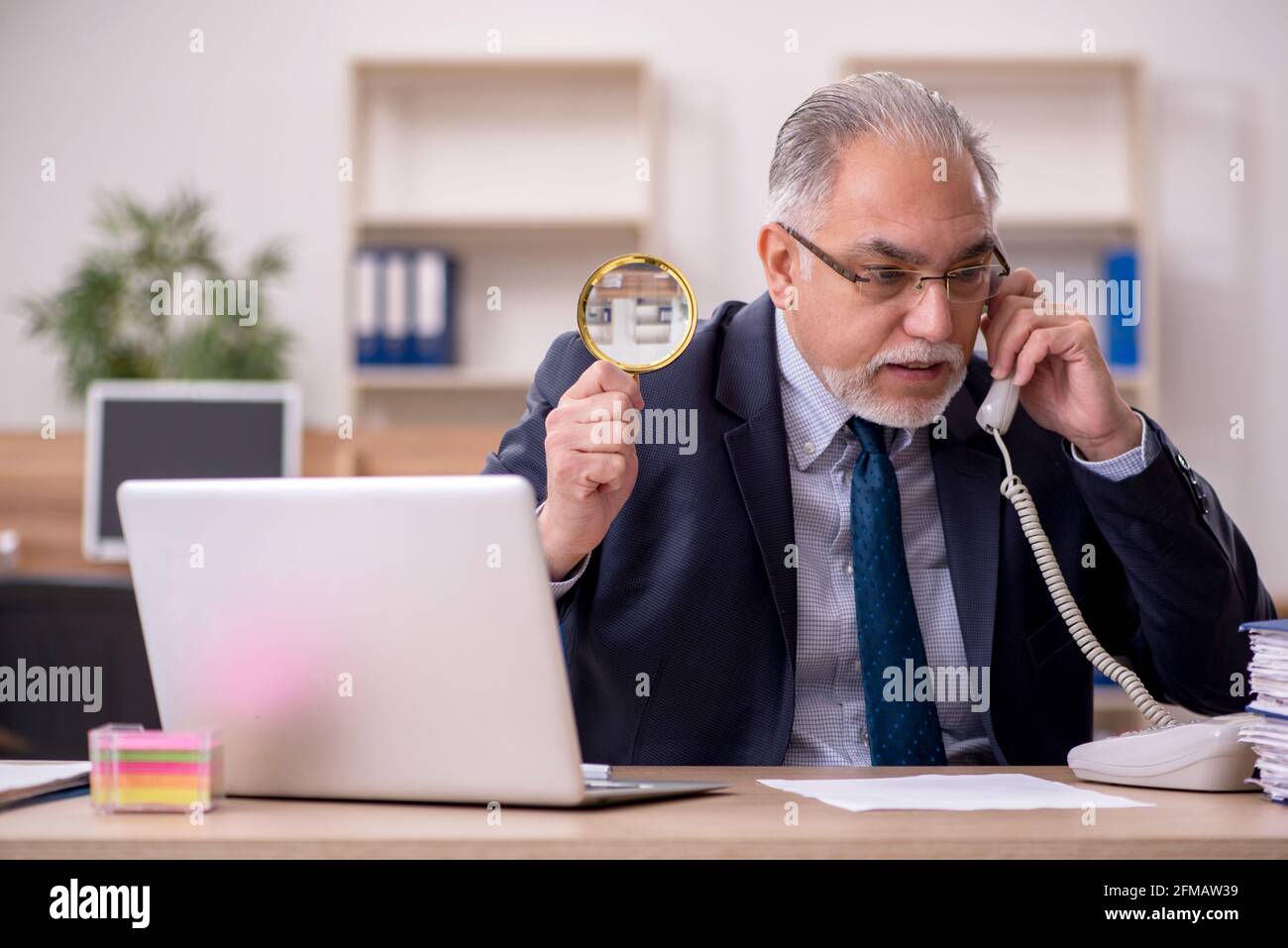 Old employee auditor holding loupe at workplace Stock Photo - Alamy