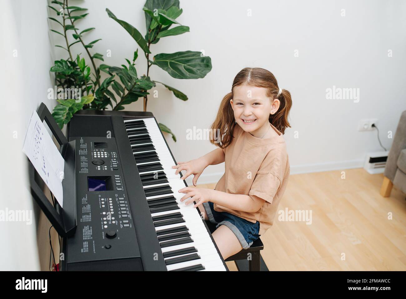 Smiling little girl enjoys playing electric piano at home. Her hair in ...