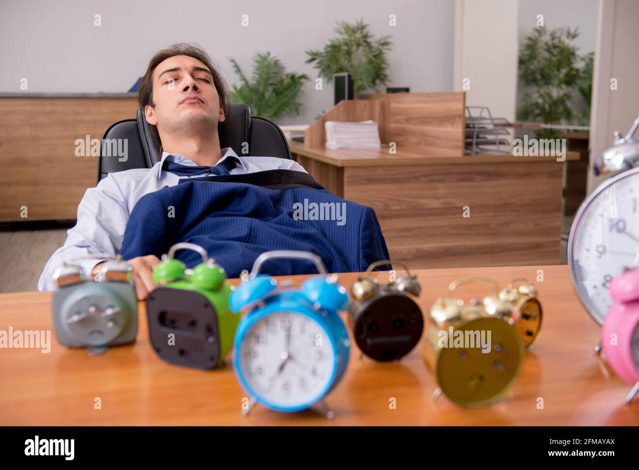 Young businessman sleeping in the office in time management concept ...