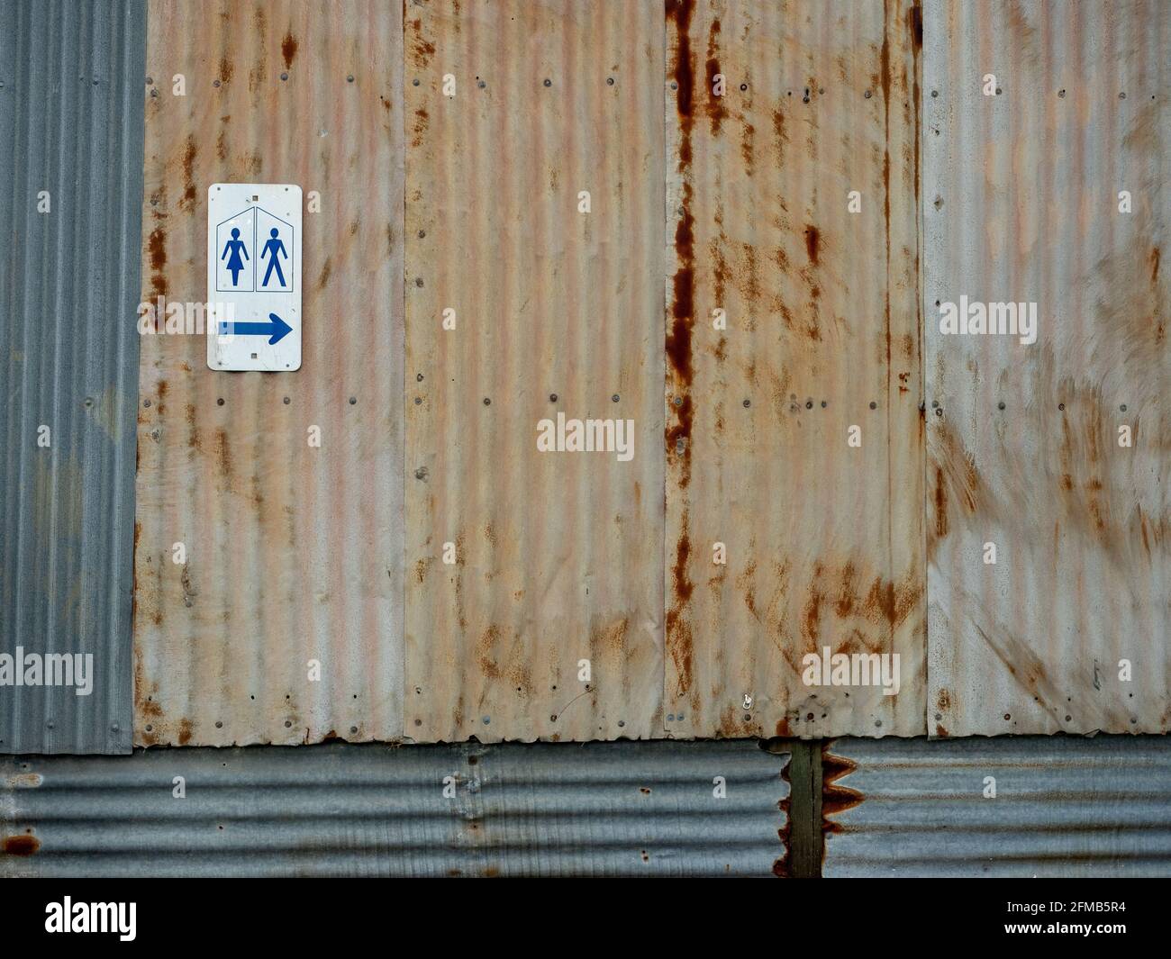 Rusting tin wall with toilet sign and arrow Stock Photo - Alamy