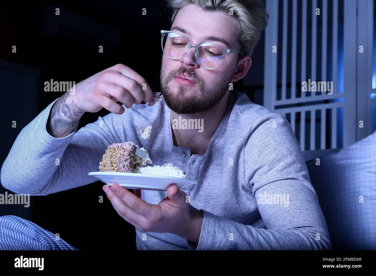 Young man eating cake while watching TV at night Stock Photo - Alamy