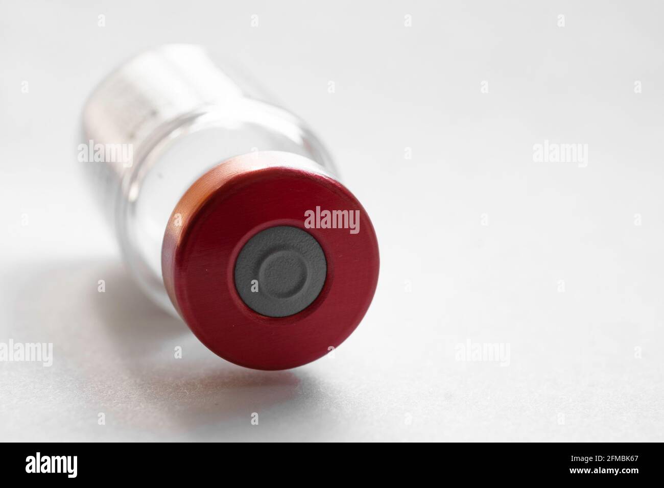 Vaccine bottle with the red cap facing the camera lying on a white ...