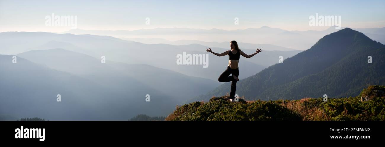 Sporty beautiful young woman doing meditation on one leg on fresh air ...