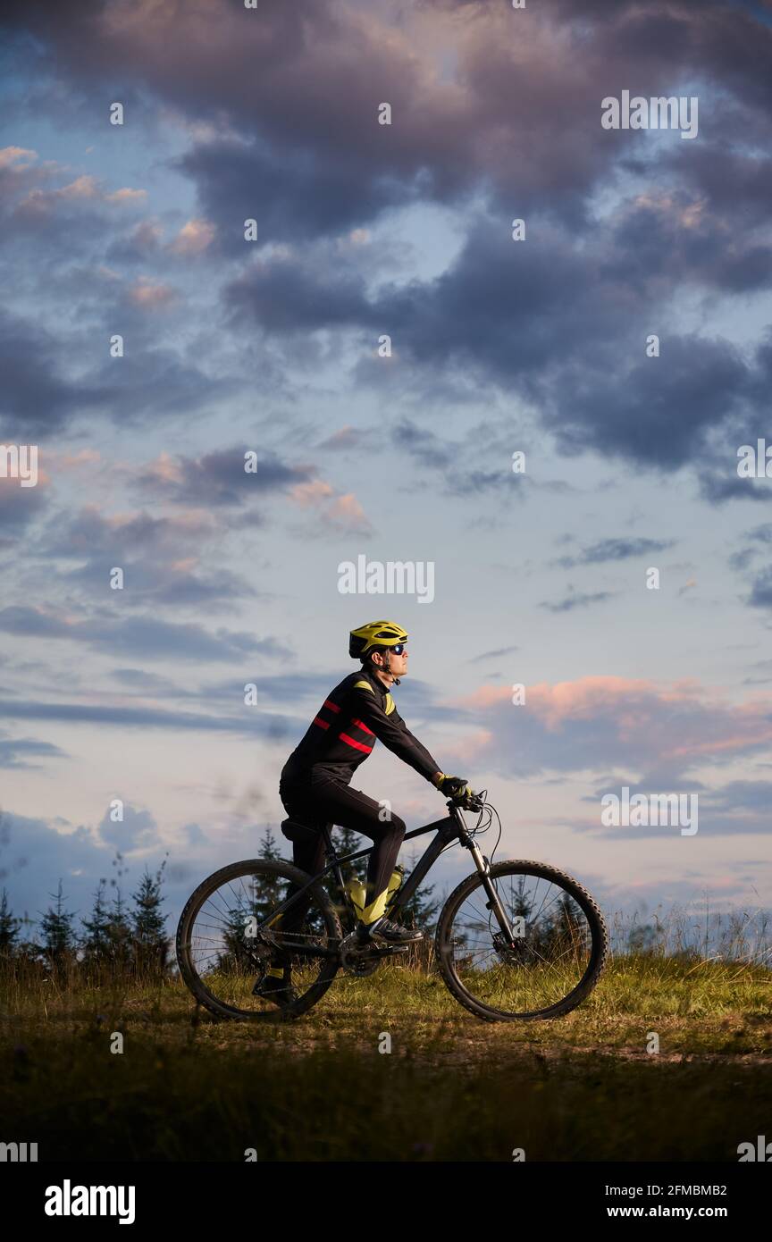 Vertical snapshot of man cyclist riding bike on sunset in the mountains ...