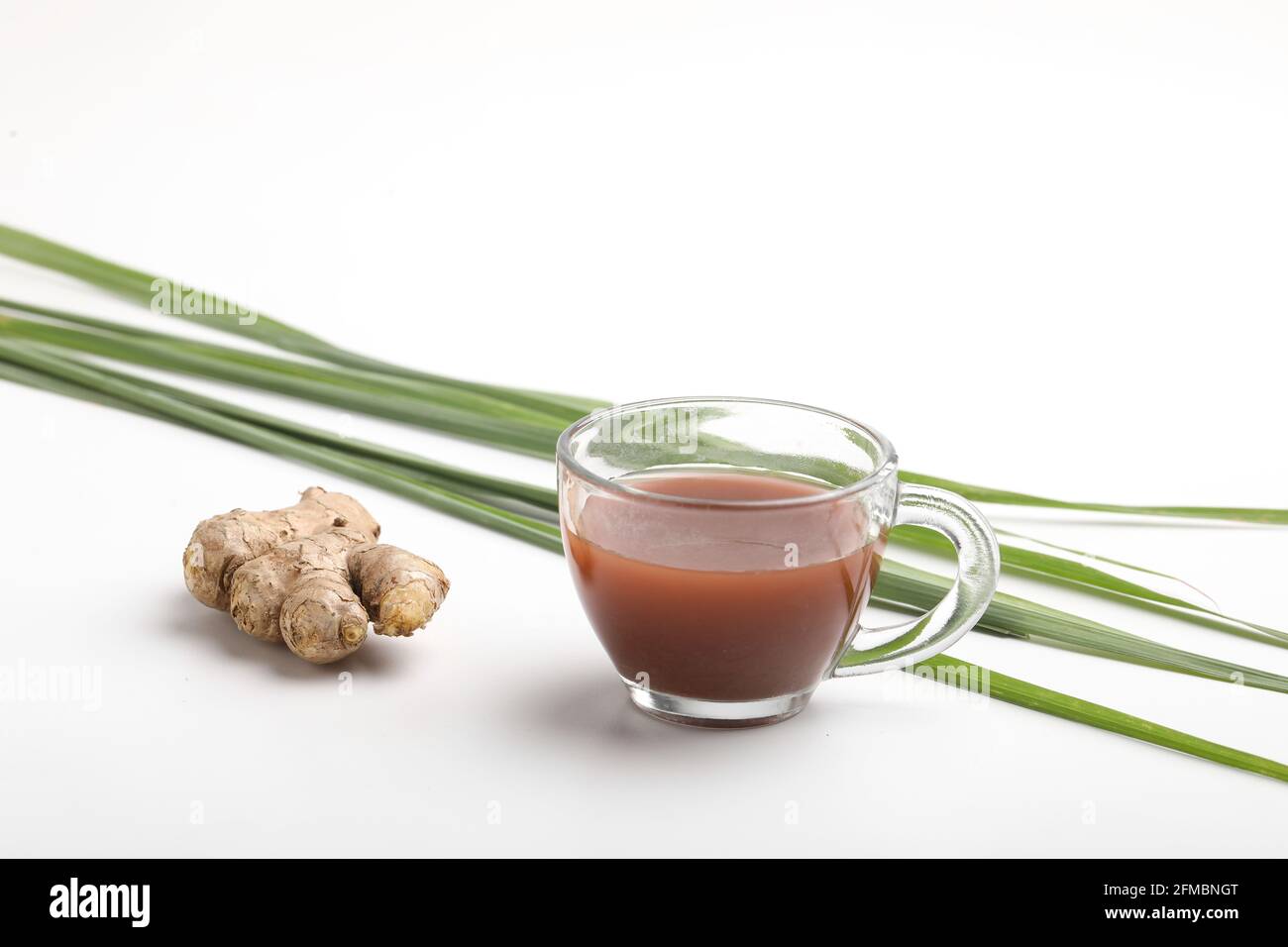 Glass cup of hot ginger tea with ginger rhizome (root) sliced on white ...