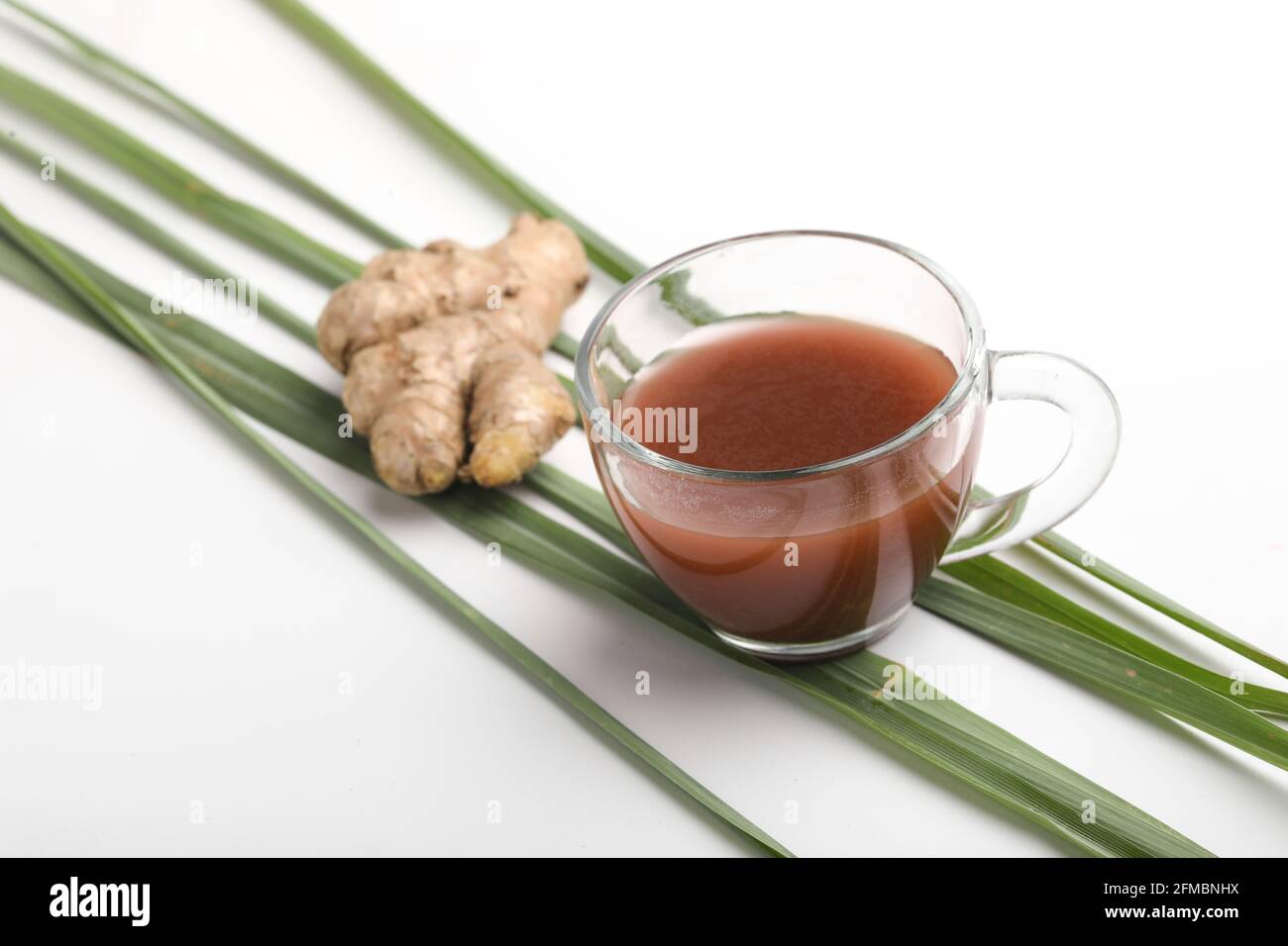 Glass cup of hot ginger tea with ginger rhizome (root) sliced on white ...