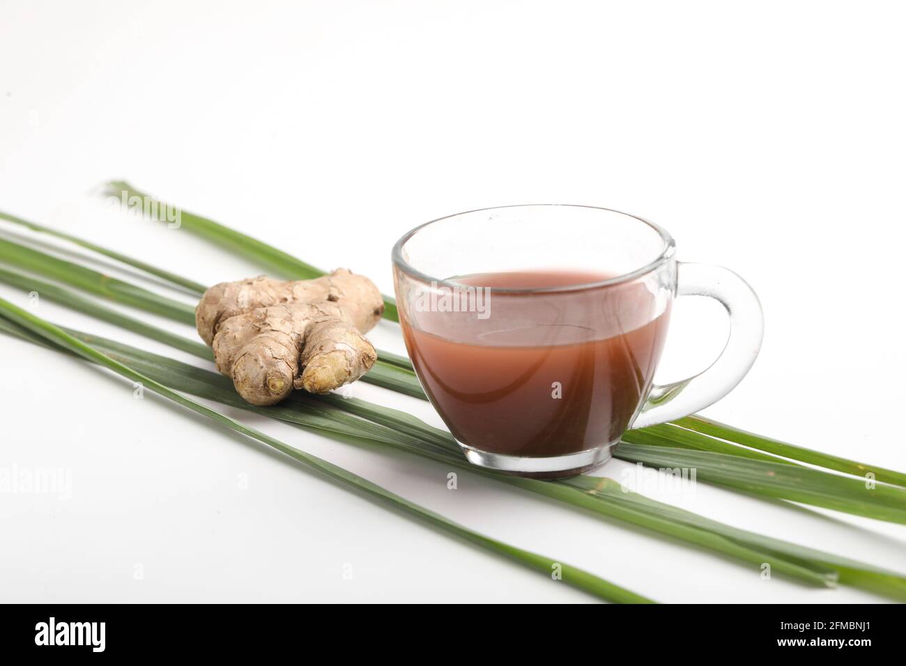Glass cup of hot ginger tea with ginger rhizome (root) sliced on white ...