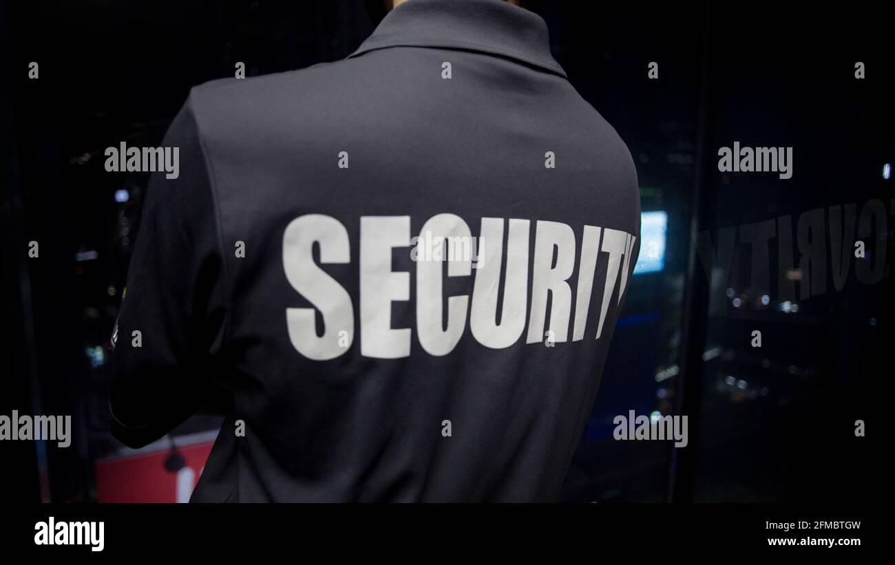 A rear view of a security guard looking down the city full of lights at ...