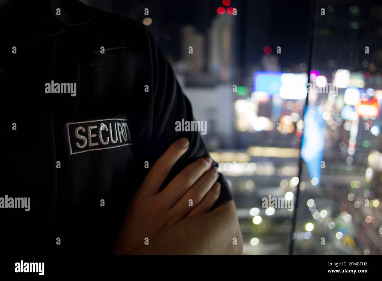 A rear view of a security guard looking down the city full of lights at ...