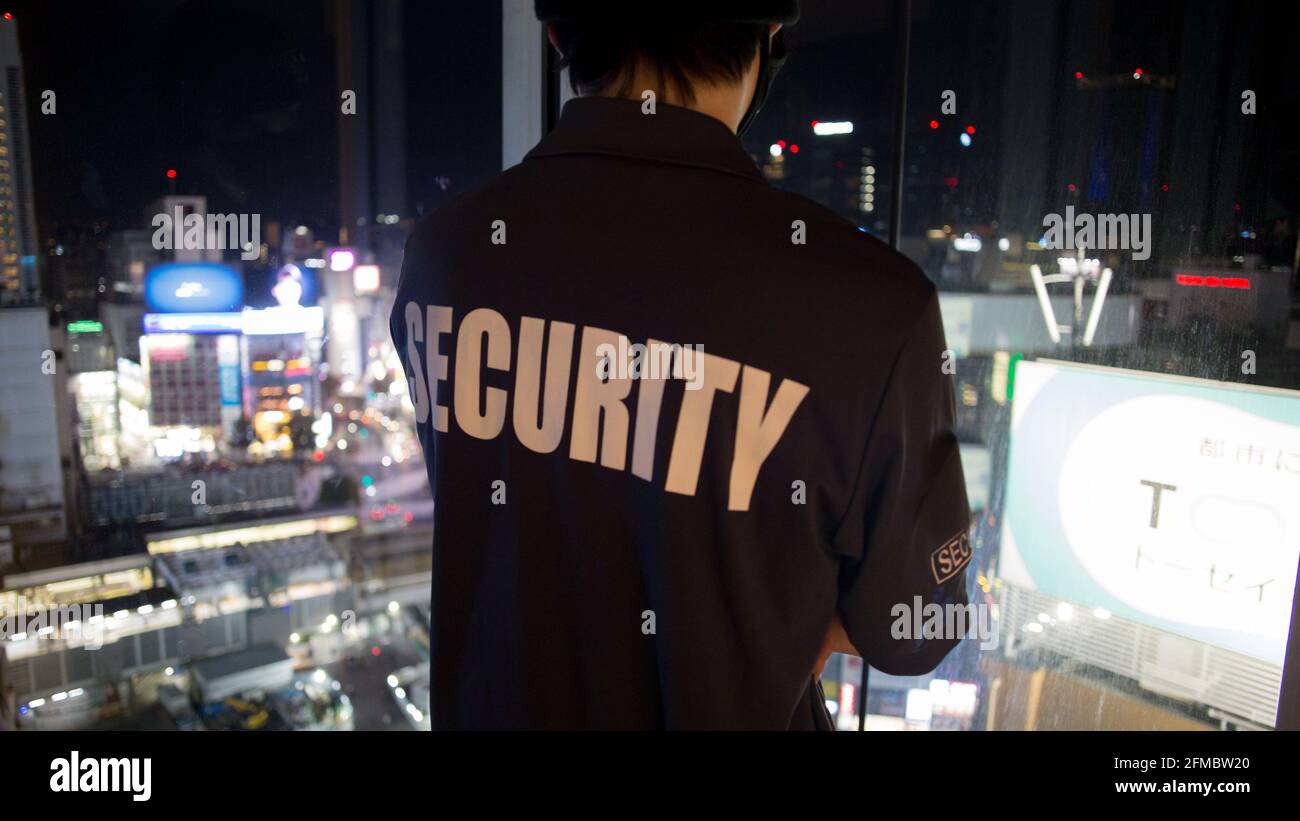 A rear view of a security guard looking down the city full of lights at ...