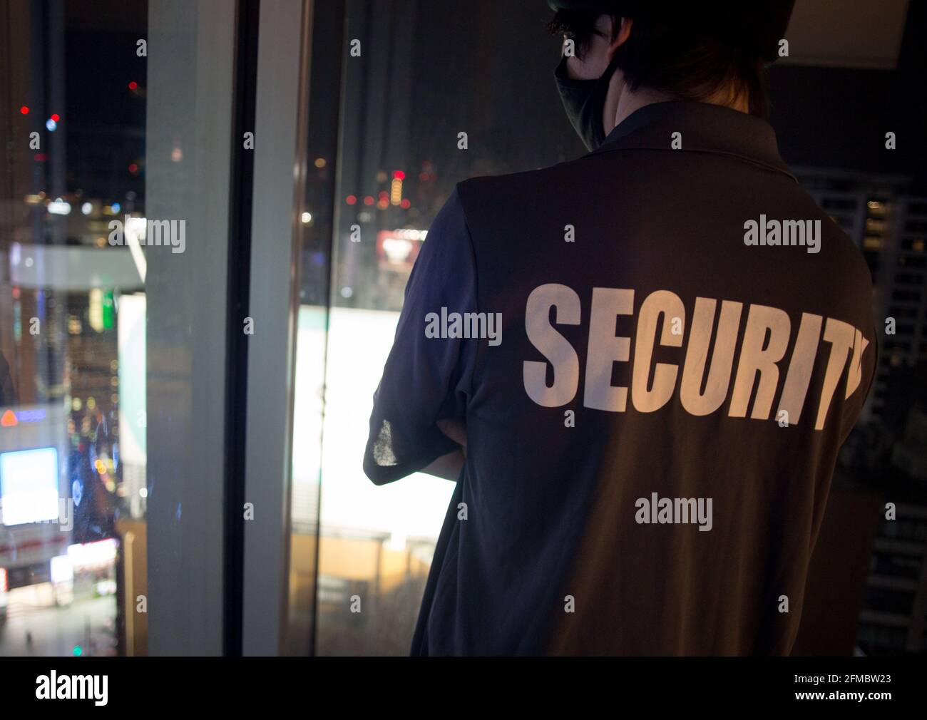 A rear view of a security guard looking down the city full of lights at ...