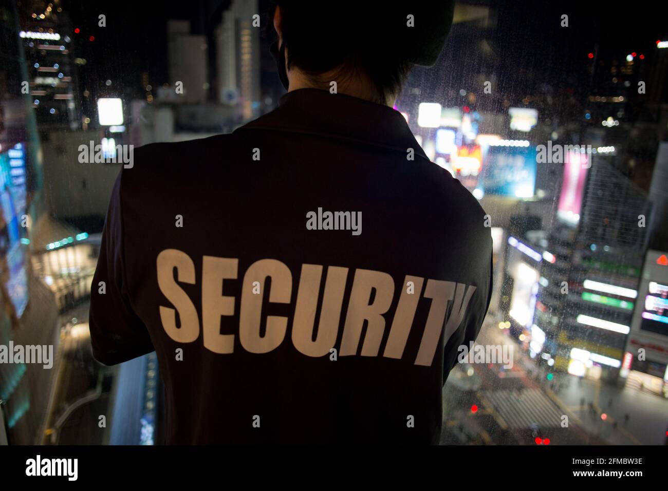 A rear view of a security guard looking down the city full of lights at ...