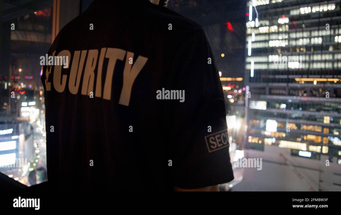 A rear view of a security guard looking down the city full of lights at ...