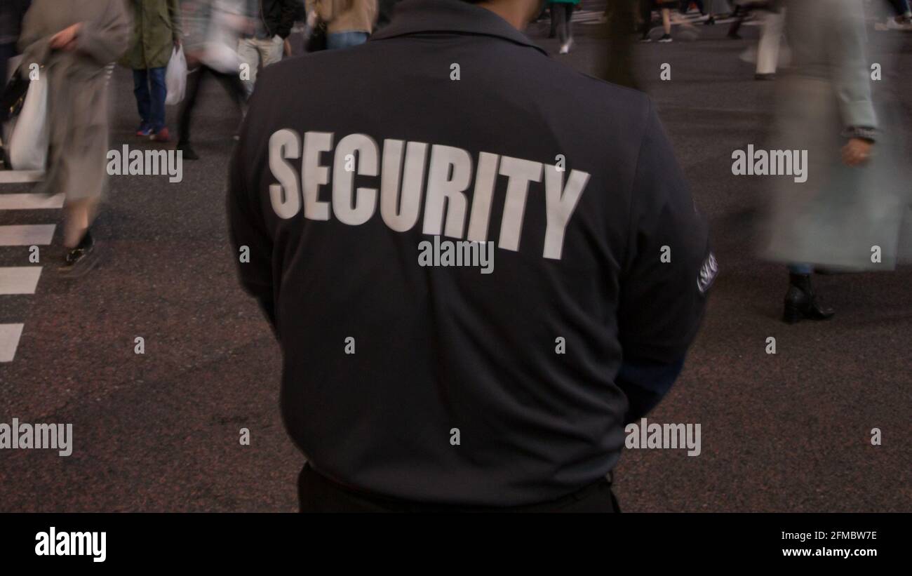 A rear view of a security guard walking through the street of the big ...