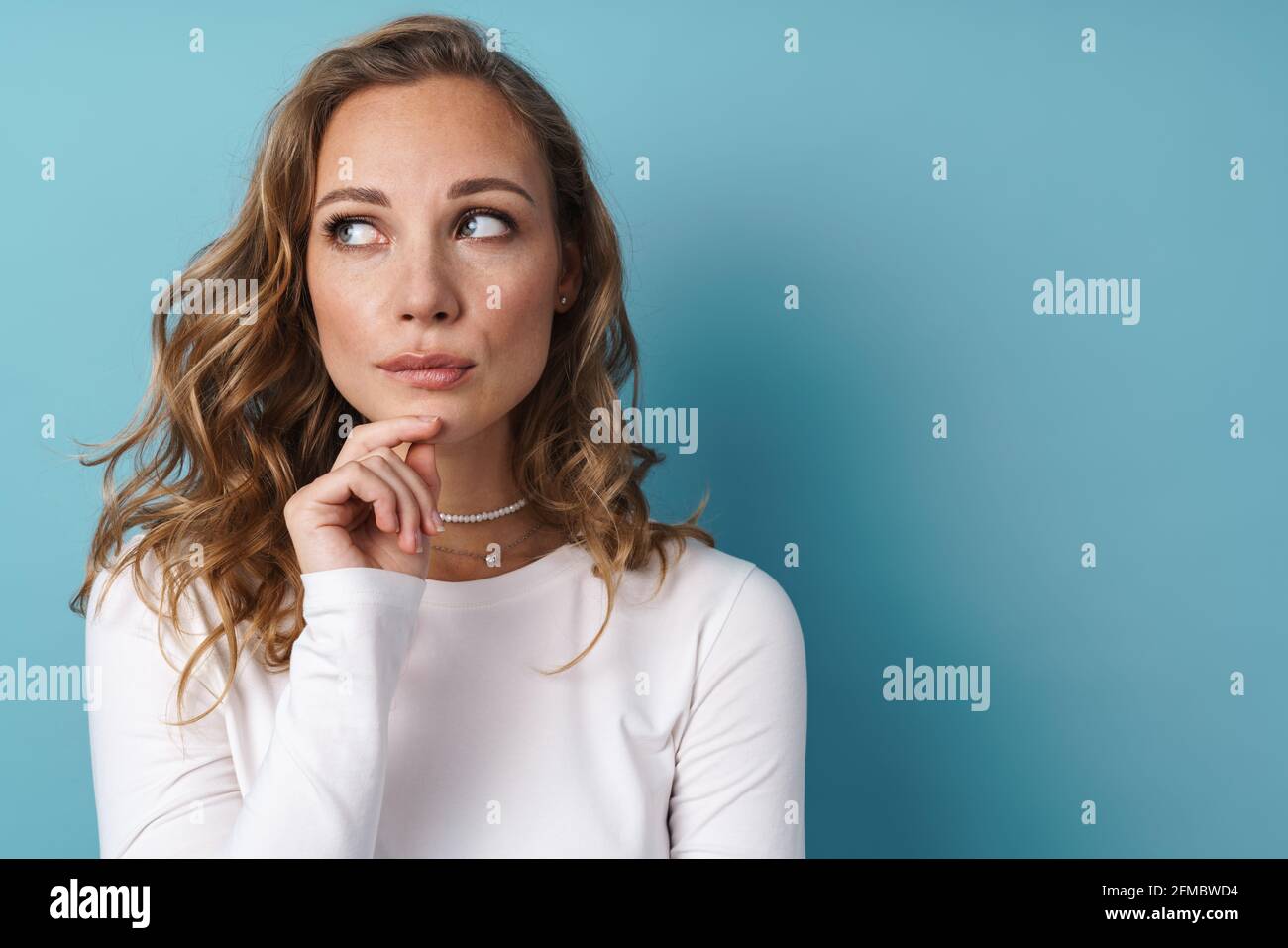 Blonde puzzled woman posing and looking aside isolated over blue wall ...