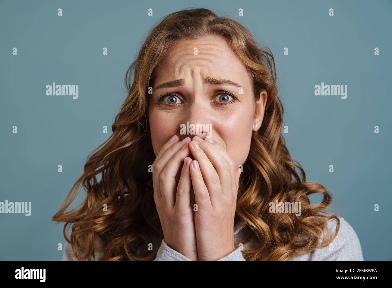 Young beautiful scared woman standing over blue background shocked ...