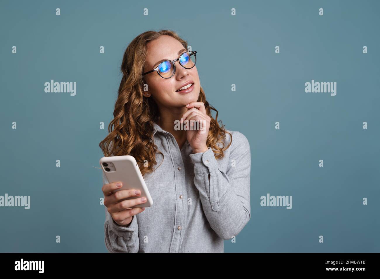 Cheerful pretty young girl usig mobile phone isolated over blue ...