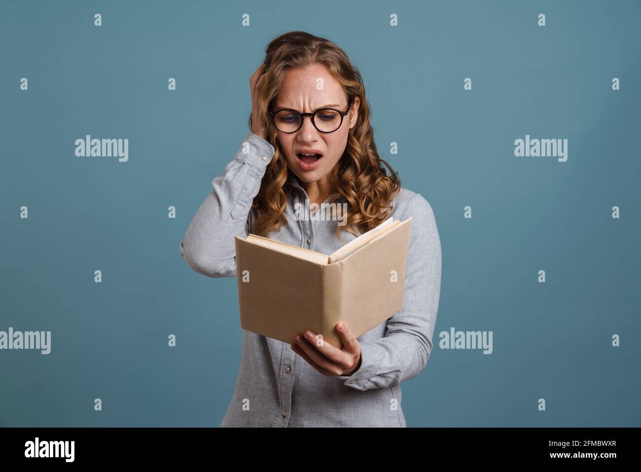 Shocked young woman reading a book while standing isolated over blue ...