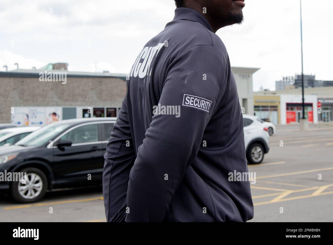 Tall black security guard in a grey uniform patrolling parking area in ...