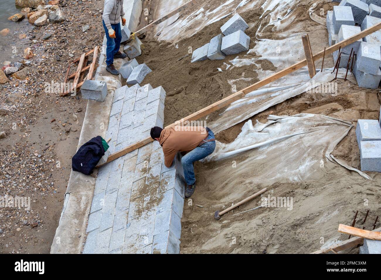 Workers installing granite natural wall stone to protect the river bank ...
