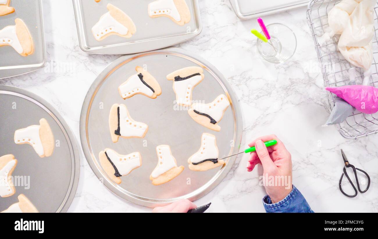 Flat lay. Decorating ice skate shaped sugar cookies with black color ...