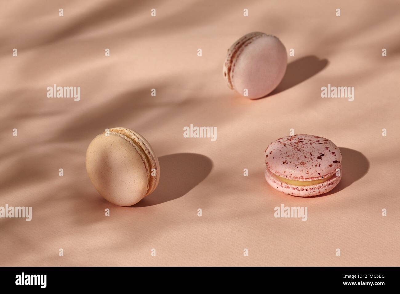Three macarons on pastel beige background with shadow Stock Photo - Alamy
