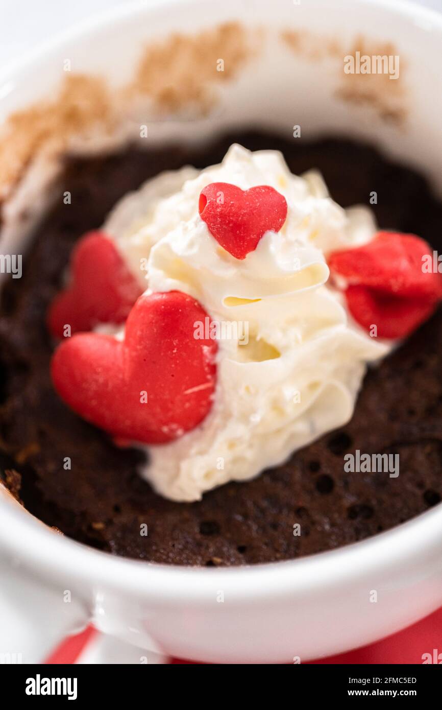 Chocolate mug cakes garnished with whipped cream and chocolate hearts ...