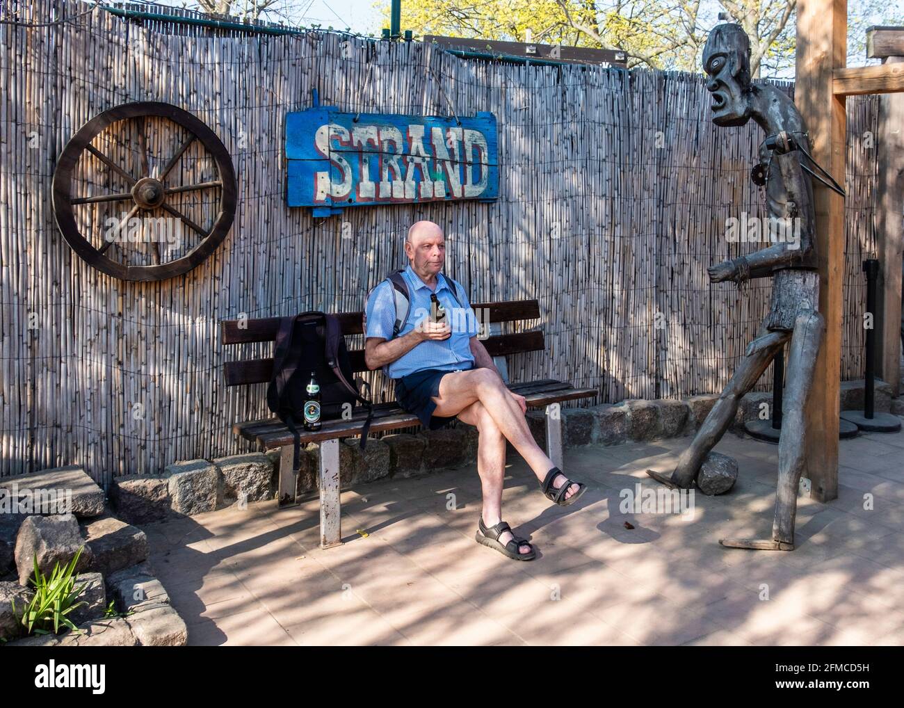 Elderly man sits on bench drinking beer at a beer garden in Mauer Park ...