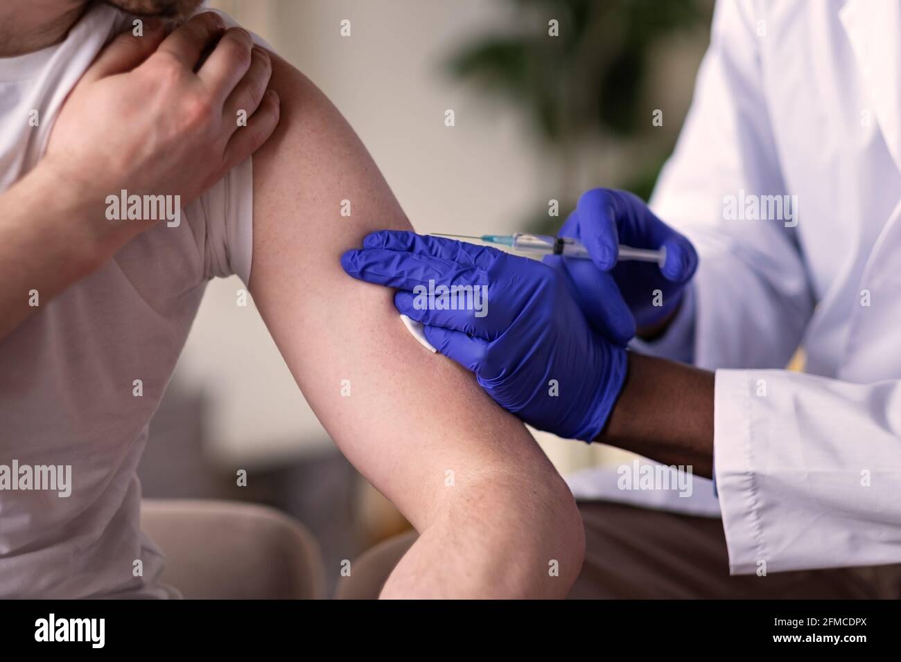 African doctor with syringe doing injection of vaccine to male patient ...