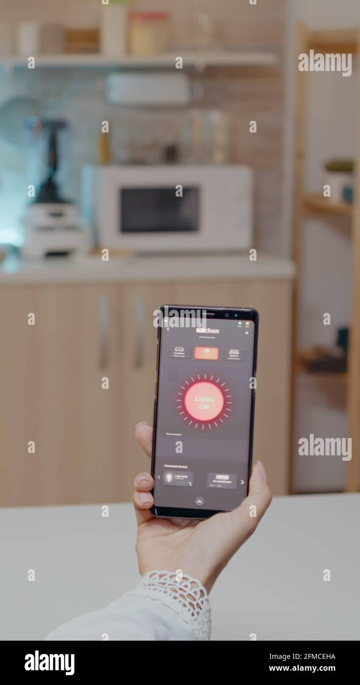 Person Looking At Mobile Phone With Lighting Controlling App Sitting In Kitchen Of House With