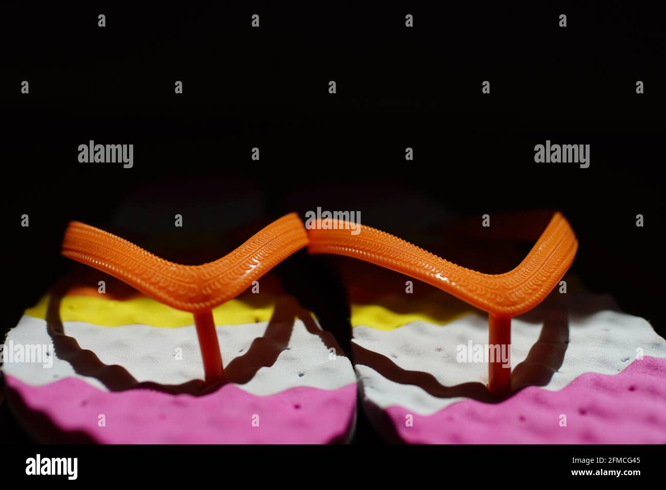 Colored beach flip flops in sunny black room. Side view Stock Photo - Alamy