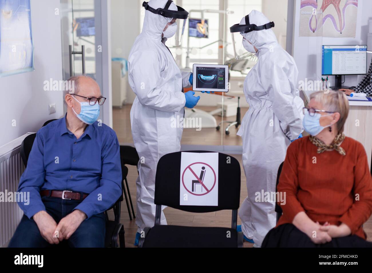 Man discussing with nurse in dental reception wearing protection suit ...