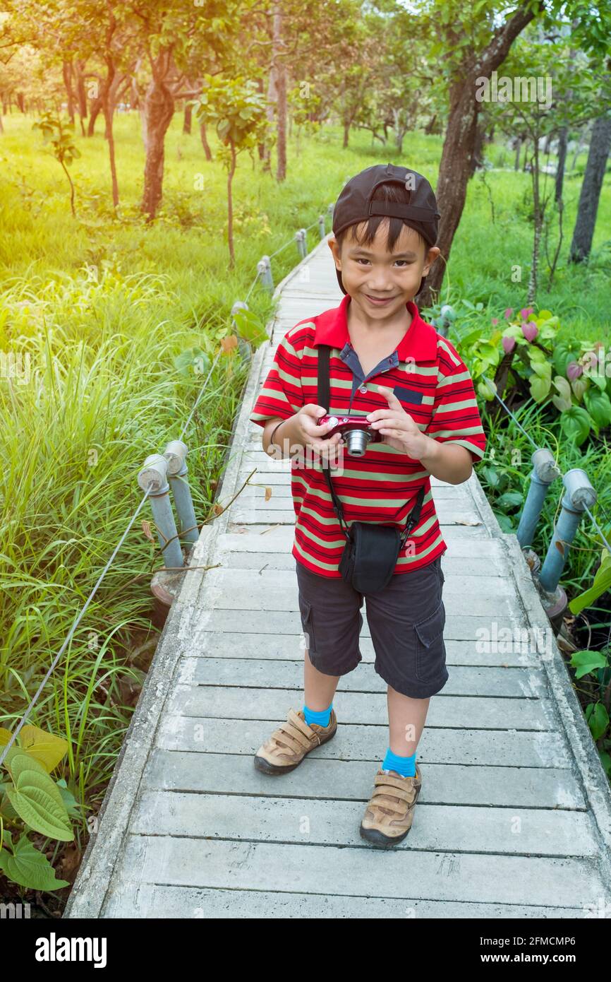 Happy asian boy with camera at national park . Child relaxing outdoors with bright sunlight at ...