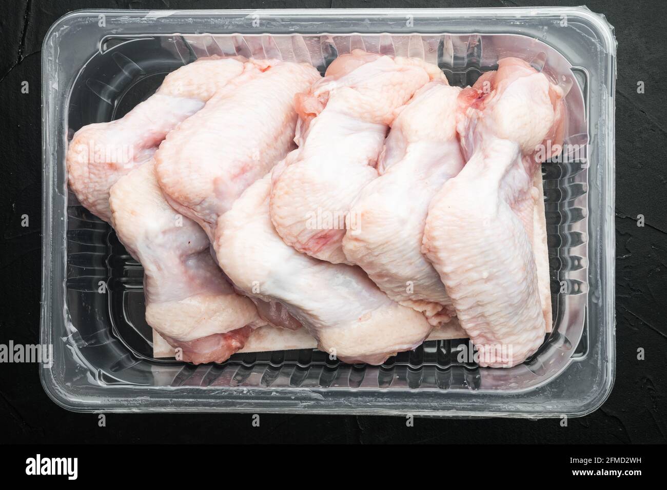 Fresh chicken wings spit in plastic vacuum pack set, on black stone ...