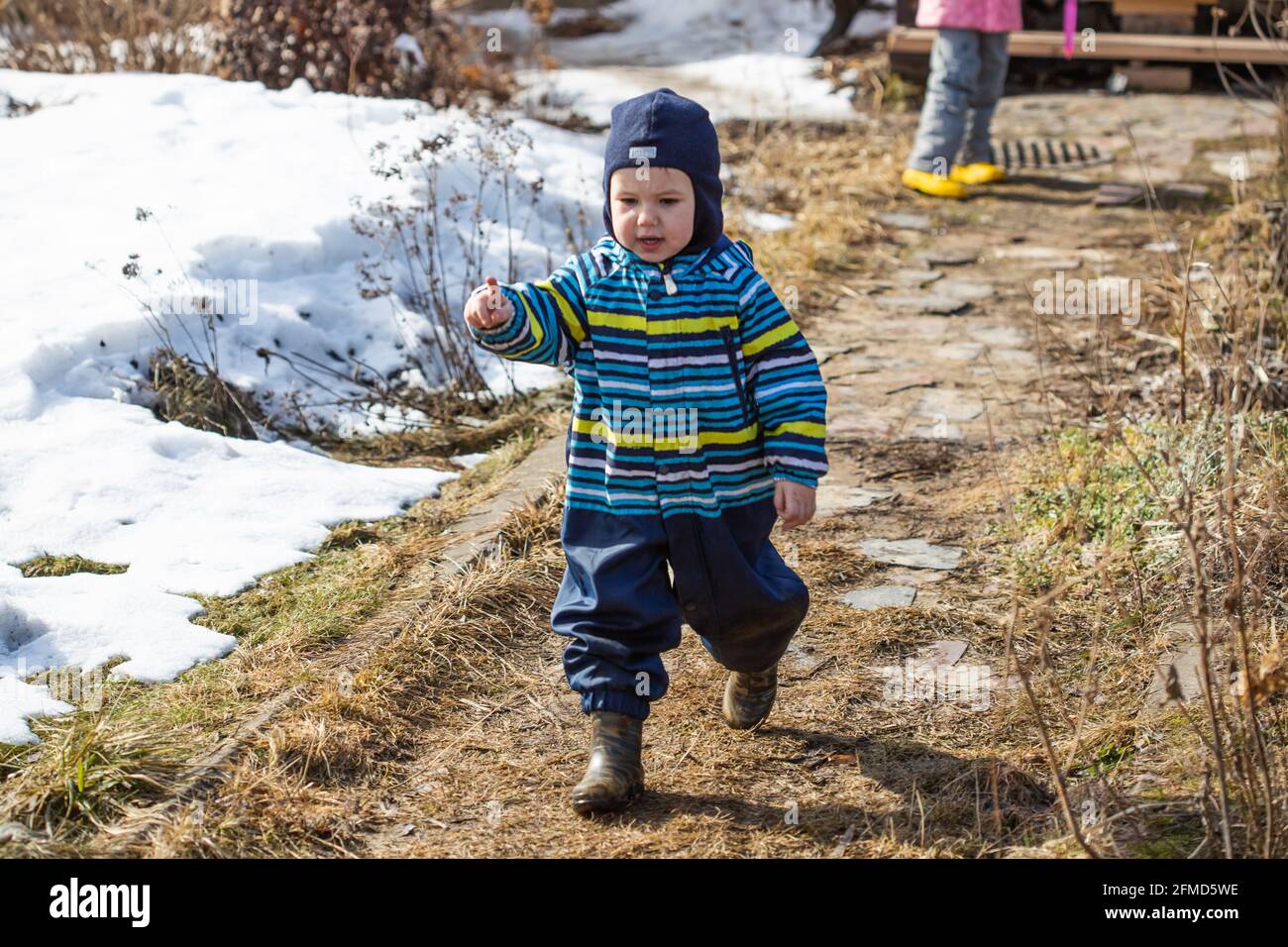 A Caucasian boy walks in the garden springtime when not all snow melted ...