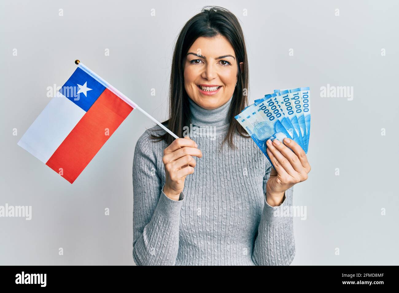 Young hispanic woman holding chile flag and chilean pesos banknotes ...