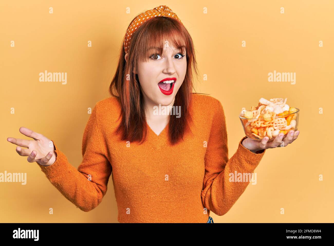 Redhead young woman holding potato chips celebrating achievement with ...