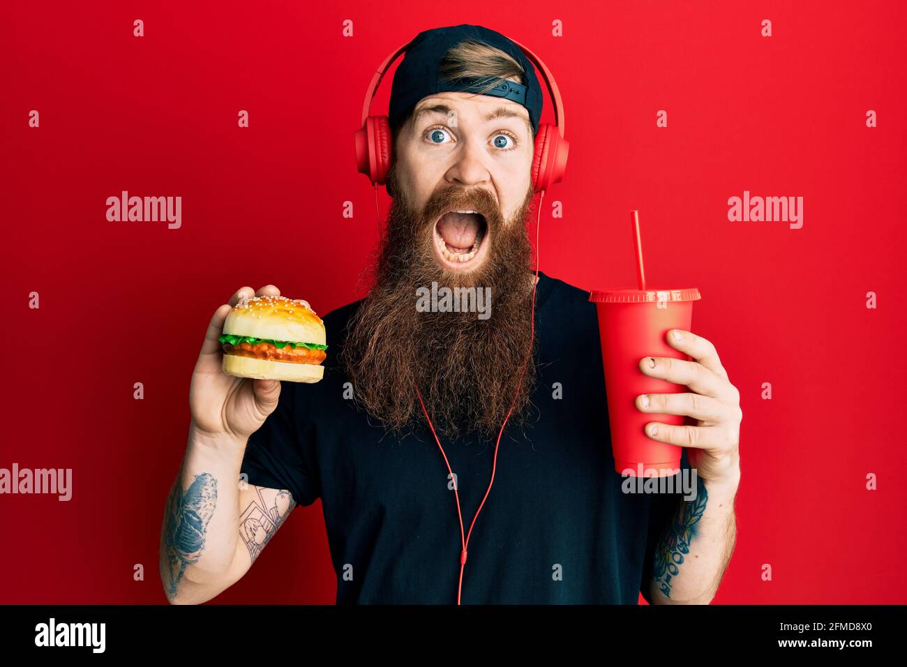 Redhead man with long beard eating a tasty classic burger and drinking ...