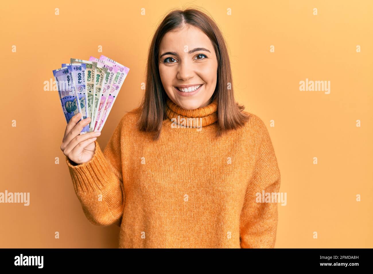 Young beautiful woman holding indian rupee banknotes looking positive ...